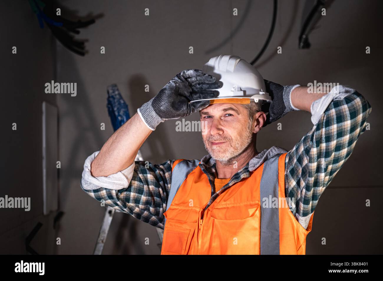 Experienced male construction worker adjusting his safety helmet on-site, wearing a high ...