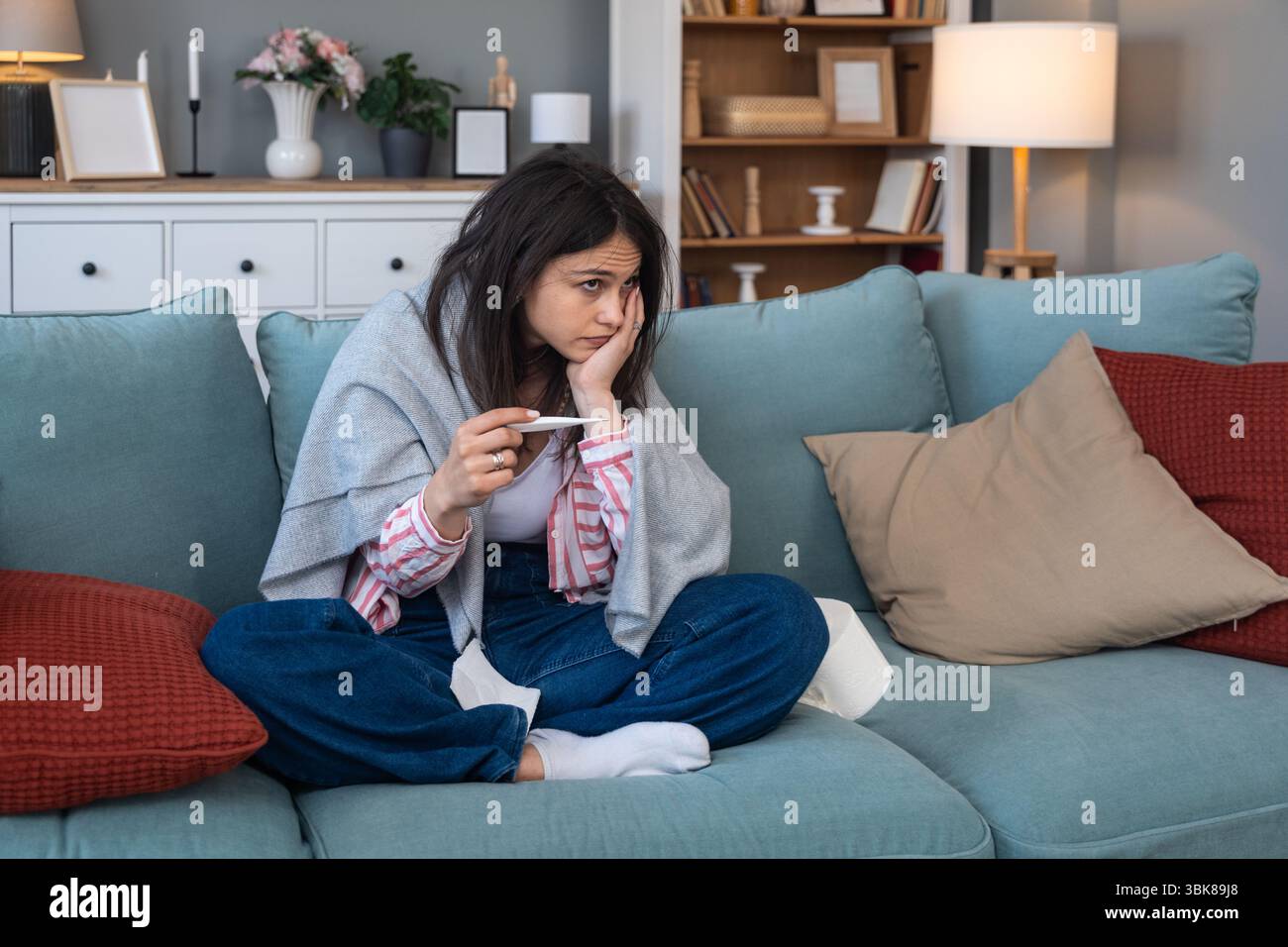 Sick woman wrapped in blanket measuring body temperature with ...