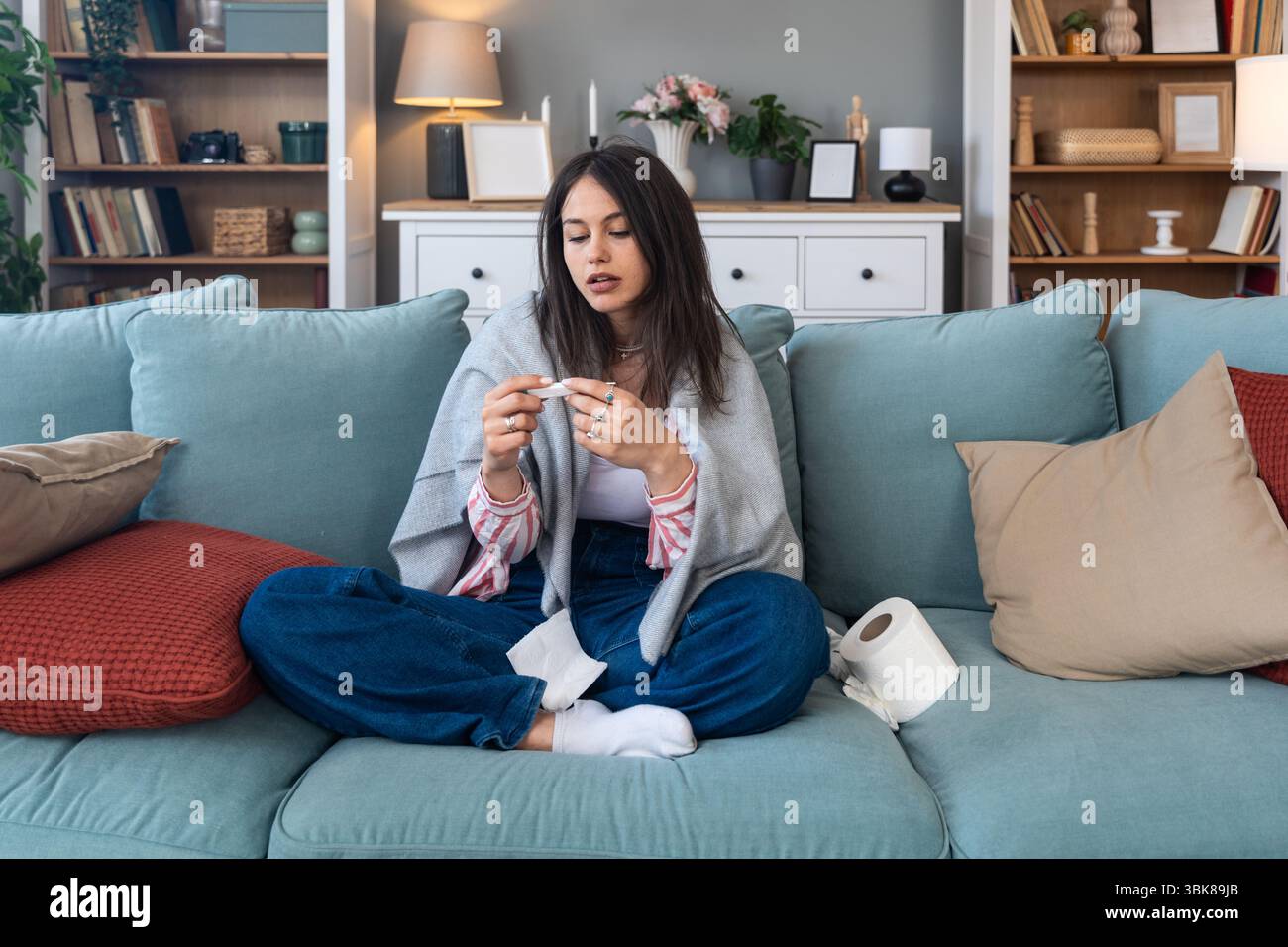 Sick woman wrapped in blanket measuring body temperature with ...