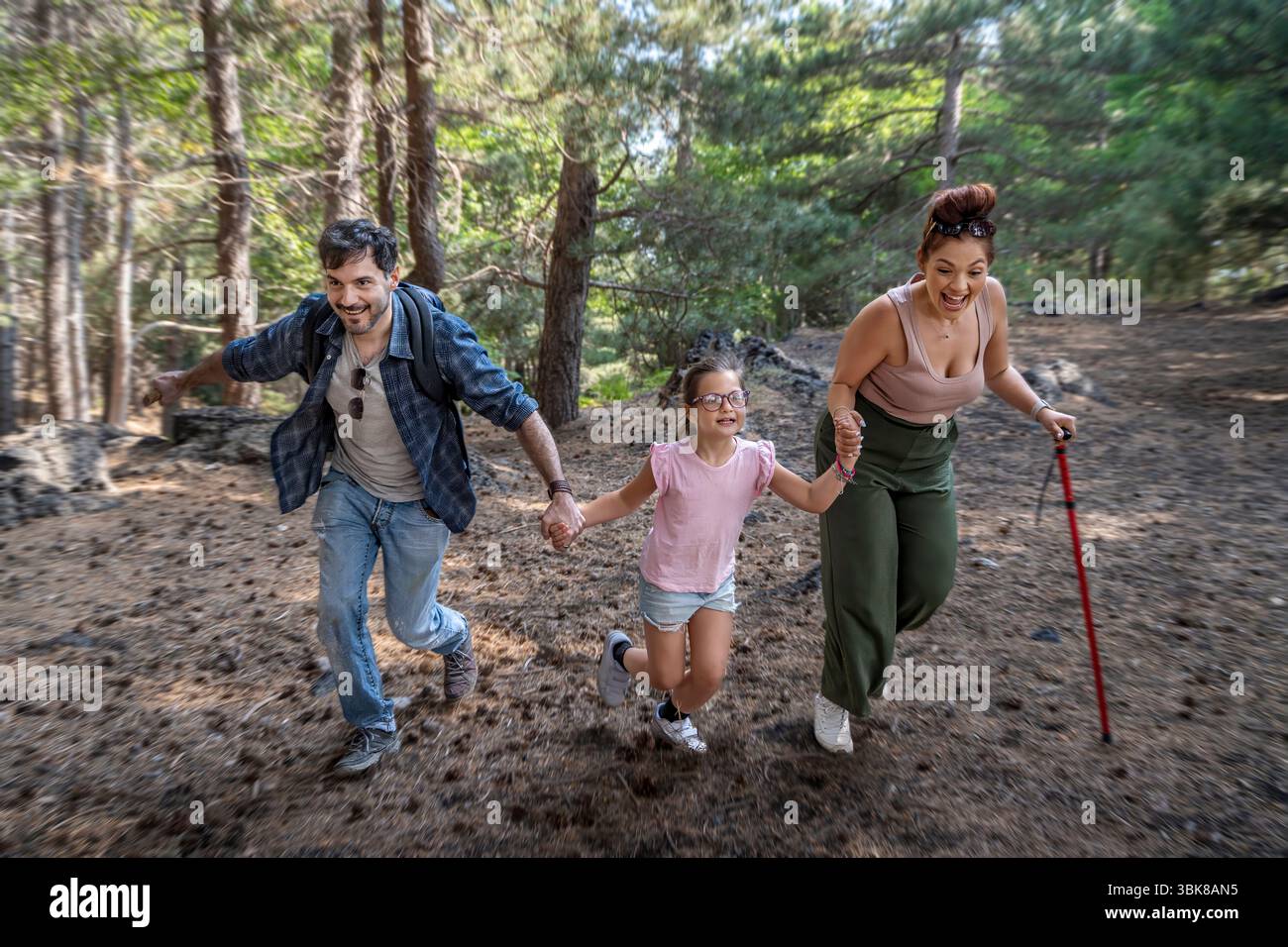 An energetic and happy family - father, mother, and daughter - hold hands and run towards the ...