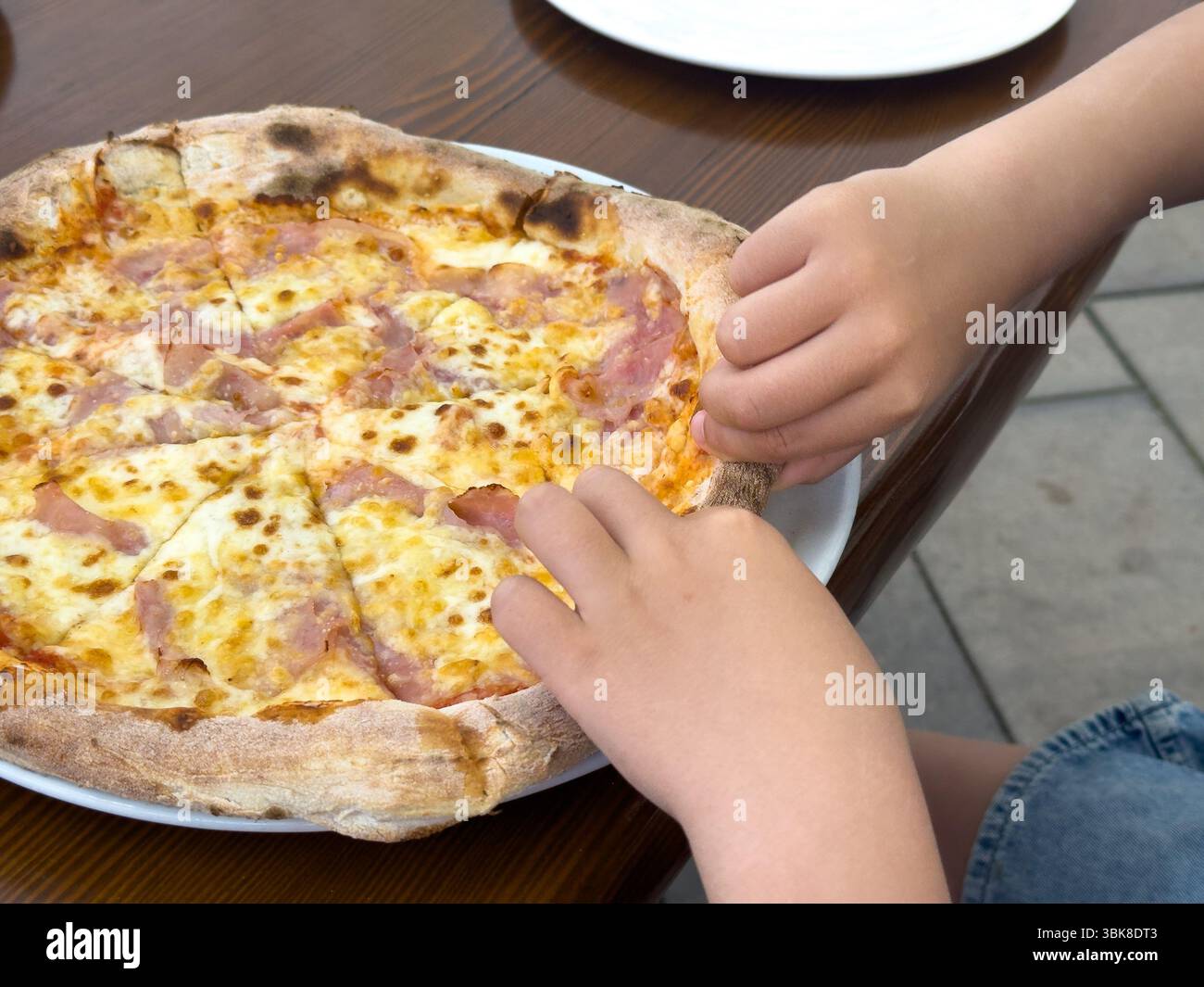 Children's hands tearing one small piece from a whole pizza in a ...