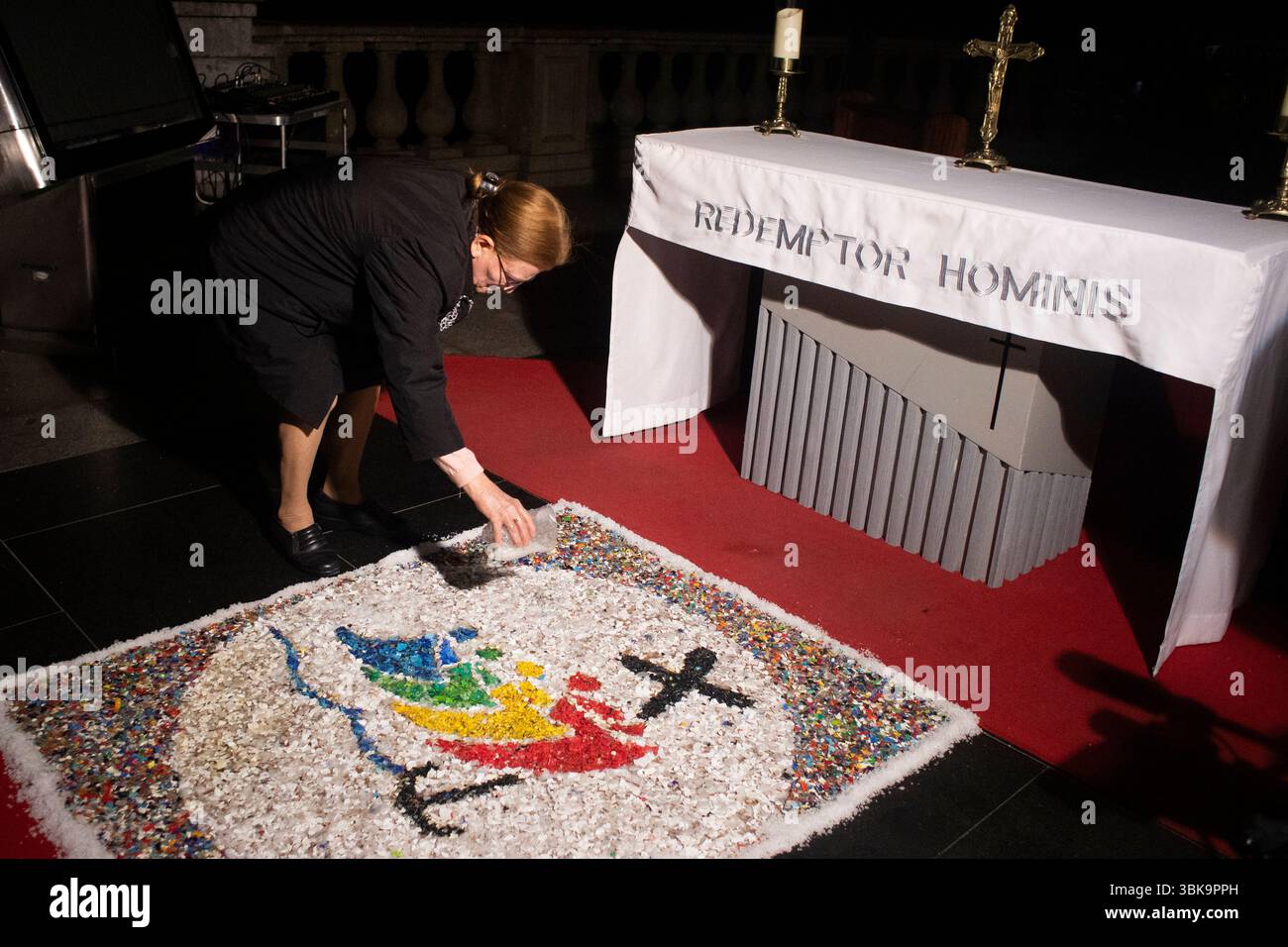 A woman puts the last touches on a rug made from plastic bottle caps ...