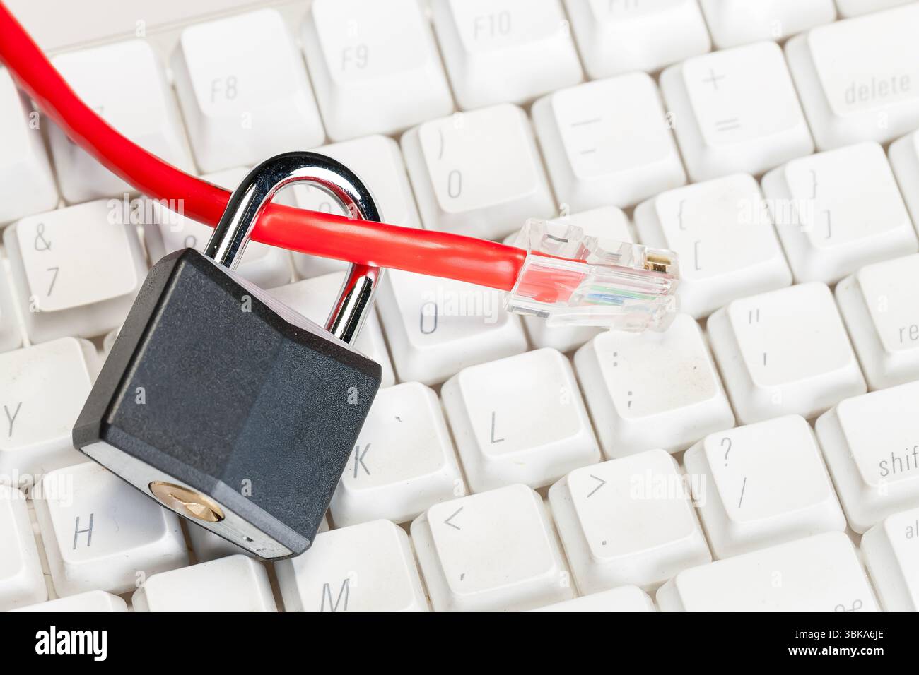 A red Ethernet cable rests atop a computer keyboard against a white ...