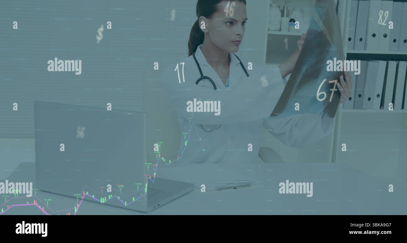 Female doctor wearing coat and stethoscope examining X-ray film in clinic, with laptop, charts ...