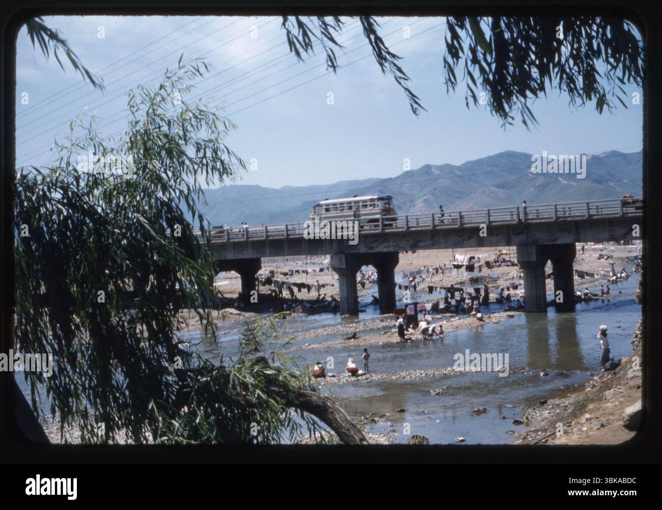 Civilians washing clothes and gathering at a river near a bridge in ...