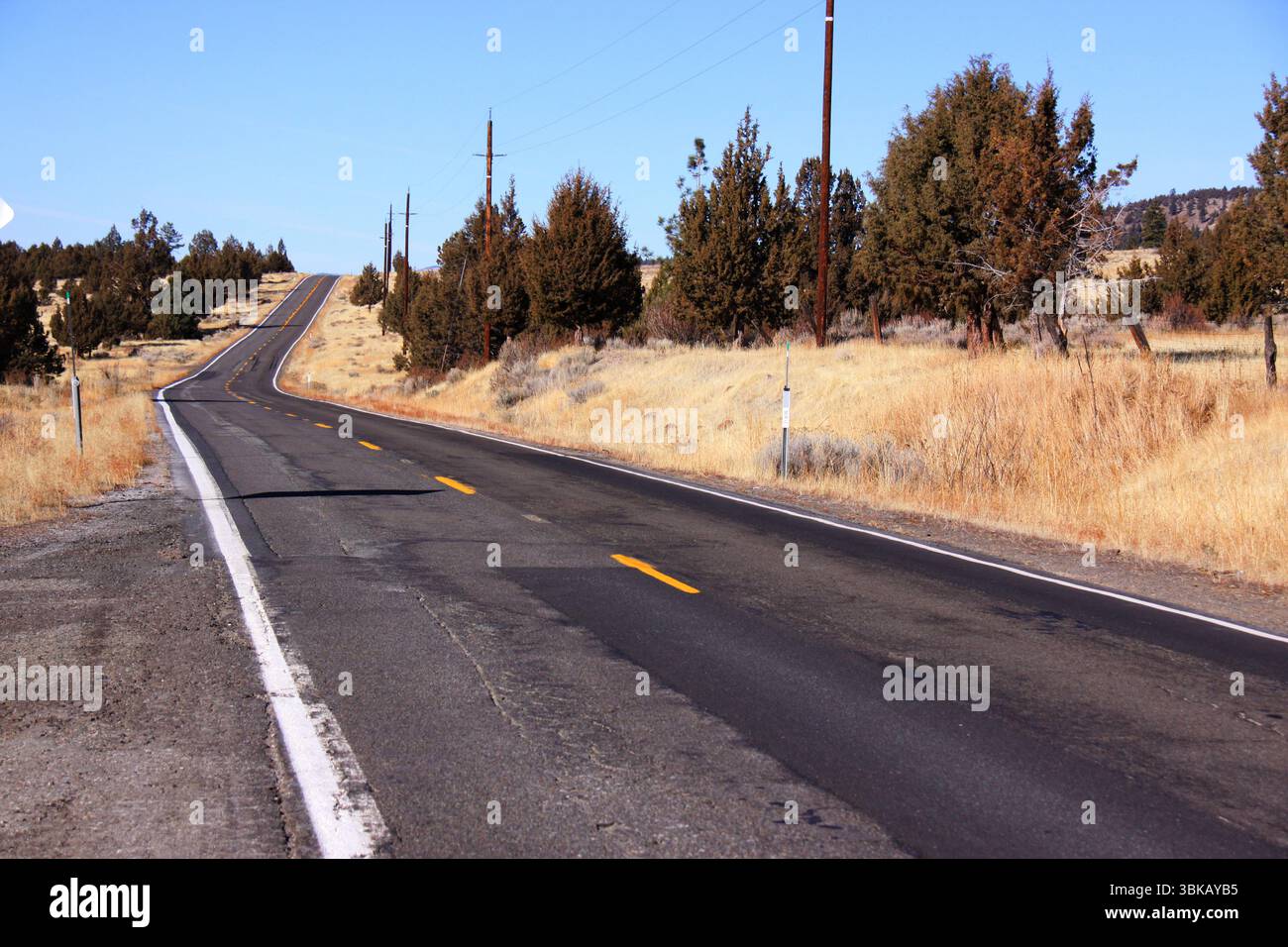 A long rural highway winds through dry grassland and juniper trees in ...
