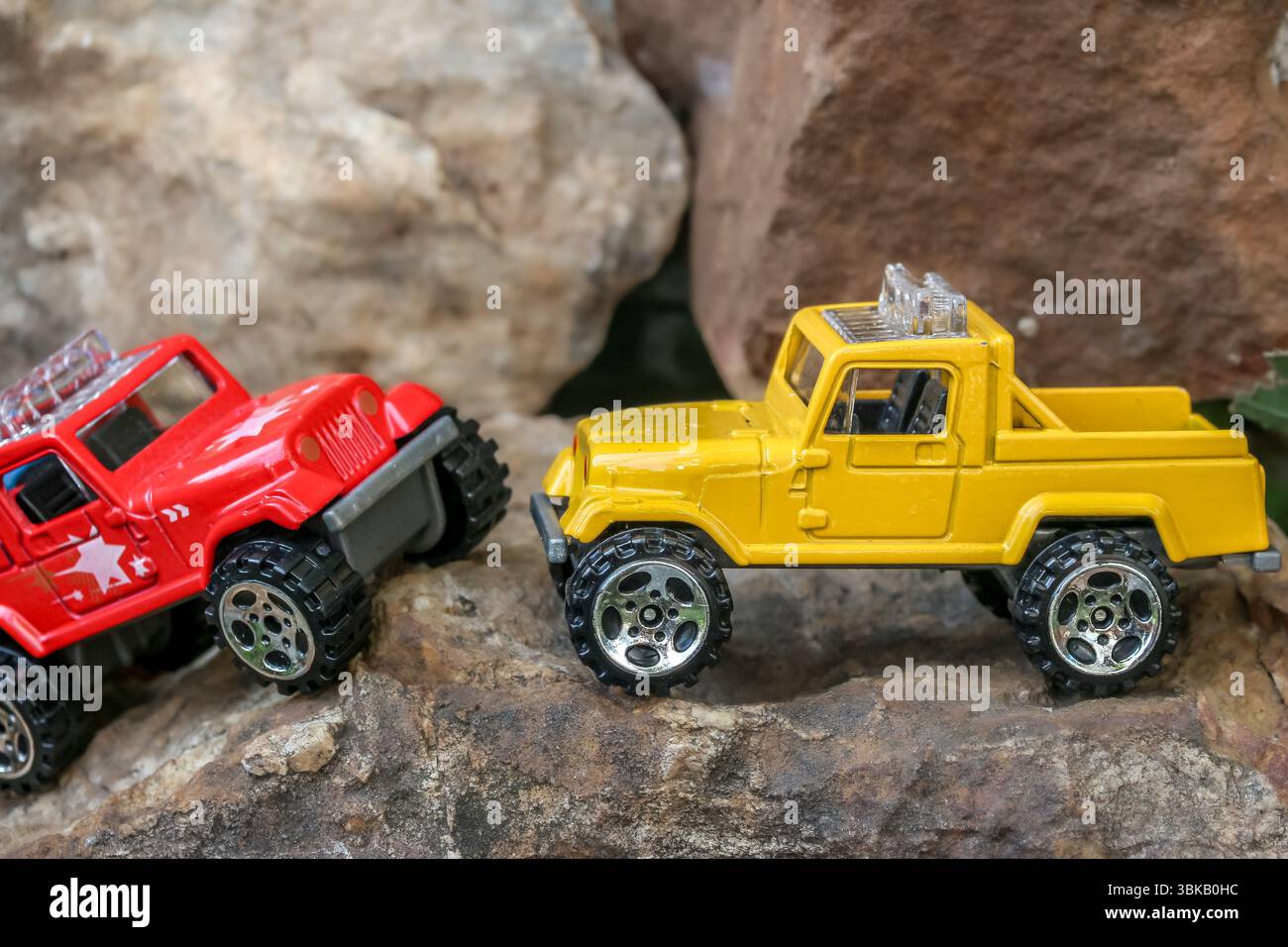 Miniature yellow & red 4x4 pickup trucks facing each other on rocky ...