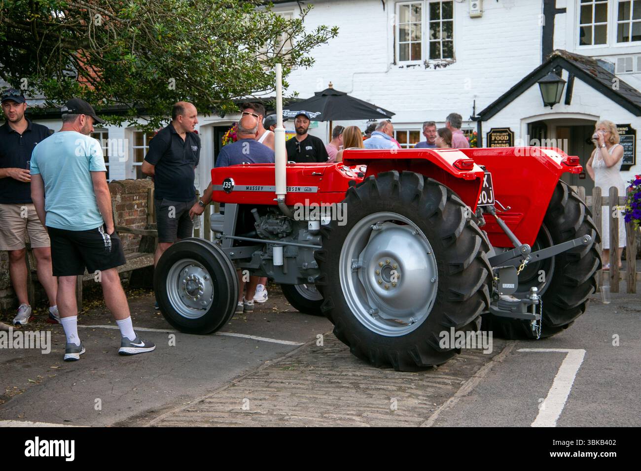 People gather around a vintage red Massey Ferguson 135 tractor ...