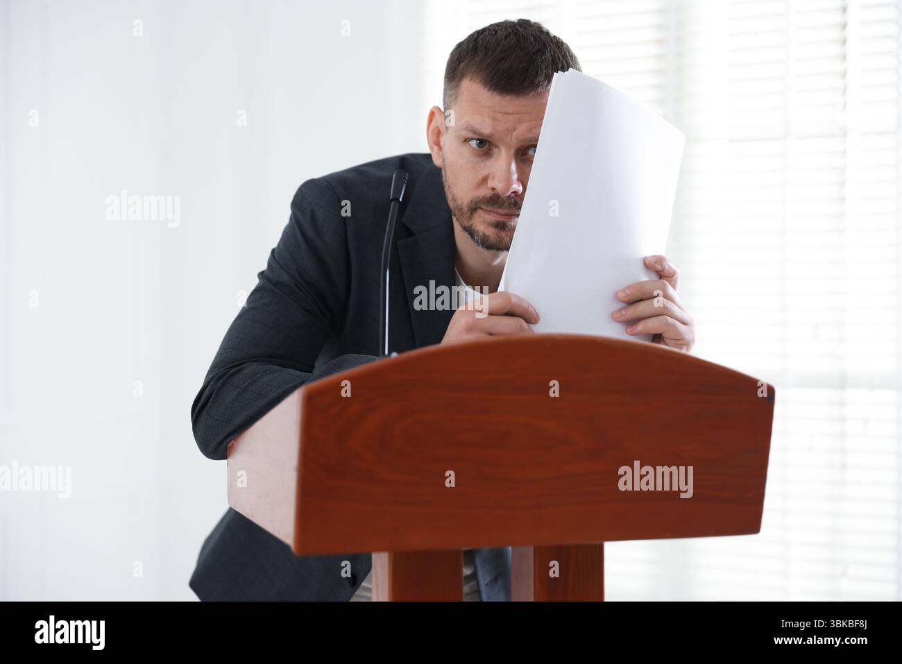 Fear of public speaking. Nervous man with microphone at lectern indoors ...