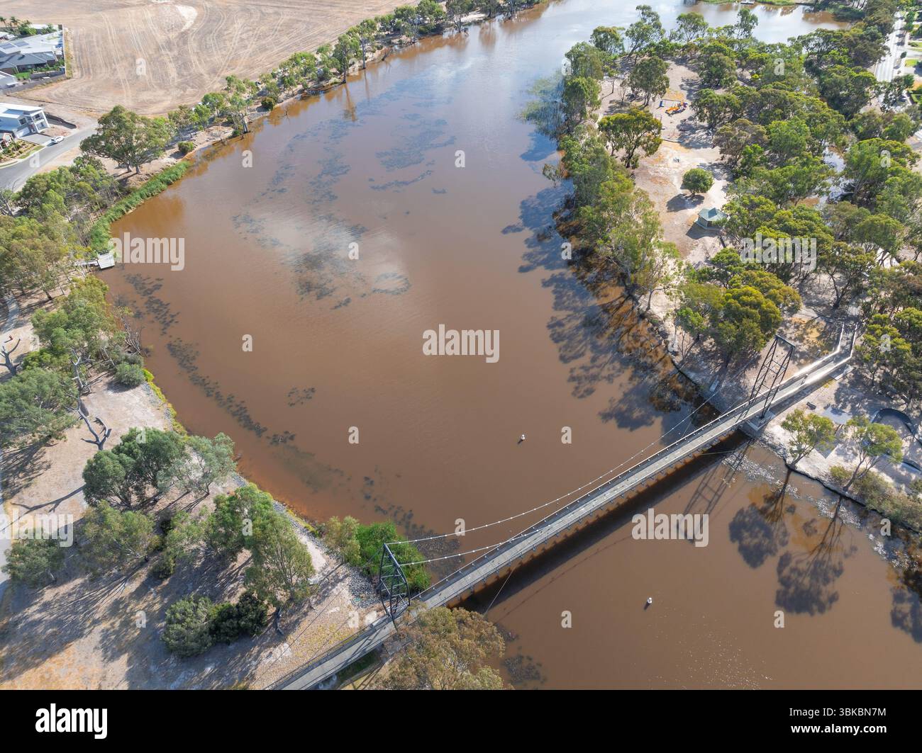 Aerial view of a pedestrian suspesion bridge over a brown river bend at ...