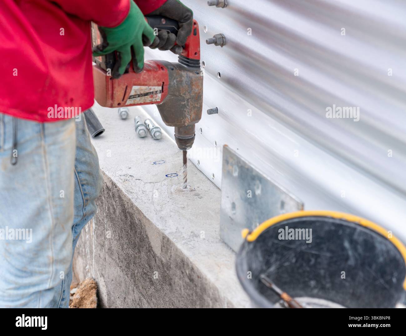 The worker is using a cordless hammer drill to drill anchor holes in ...