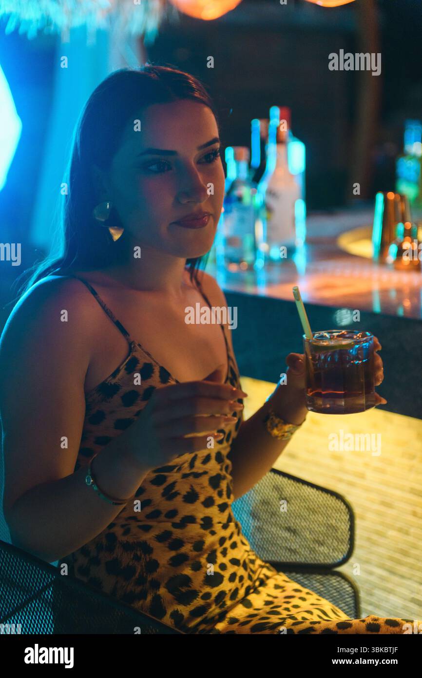 Stylish brunette woman wearing leopard print dress enjoying cocktail at elegant hotel bar Stock ...