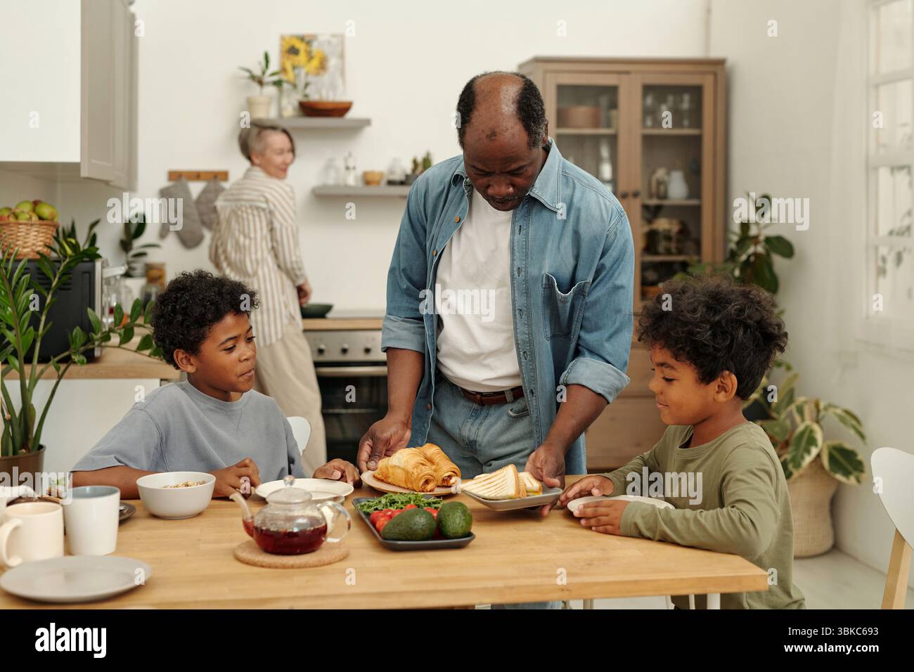 Diverse family sharing breakfast in cozy kitchen, with elder preparing ...