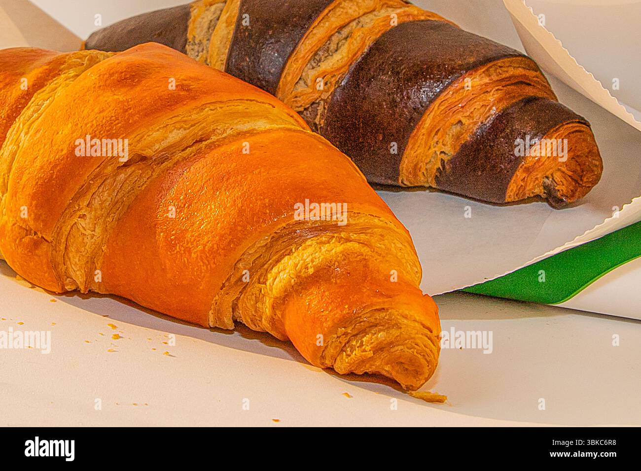 Two freshly baked croissants, one golden and one chocolate, wrapped in ...
