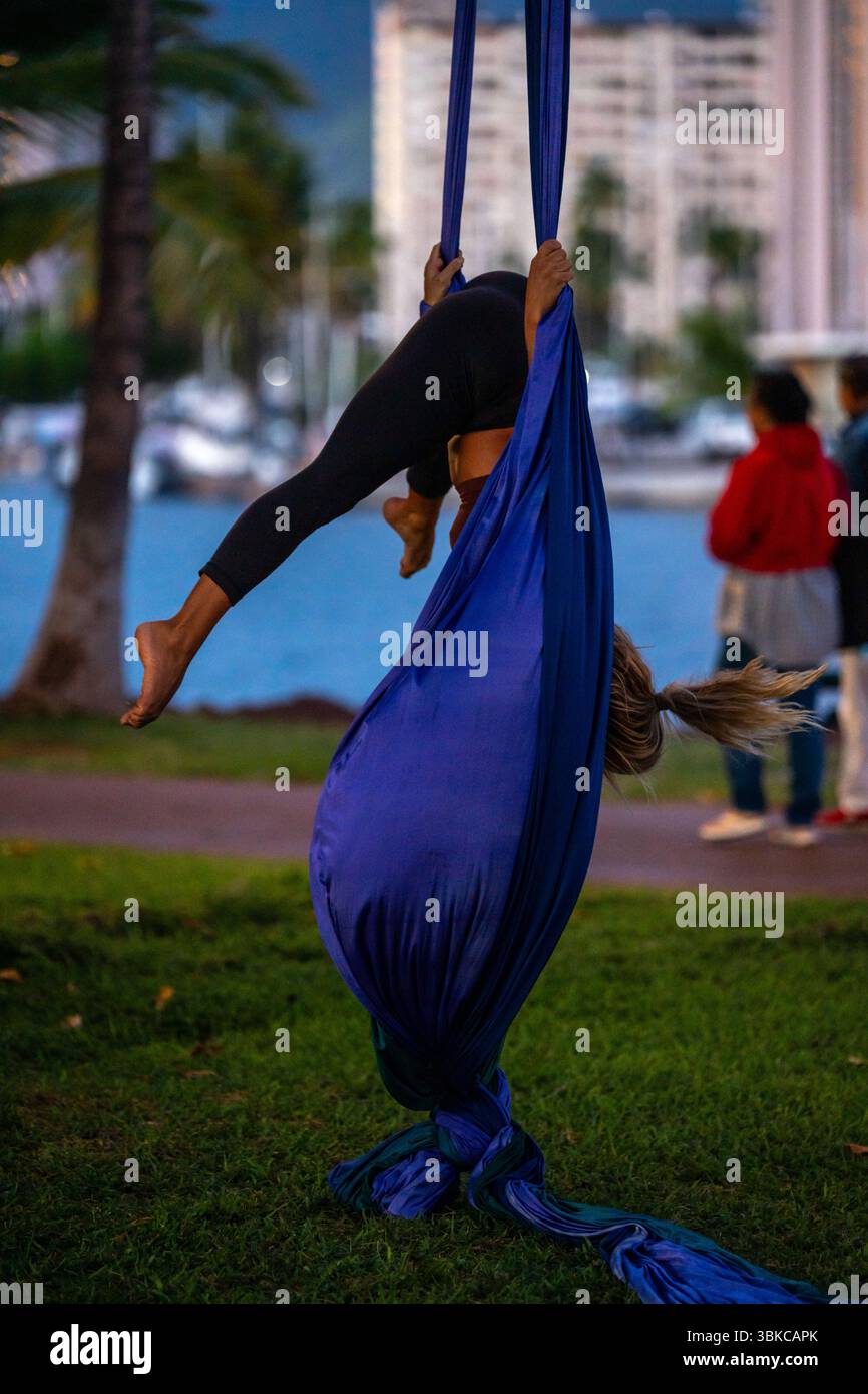 A woman practices aerial silk outdoors, suspended upside down in ...