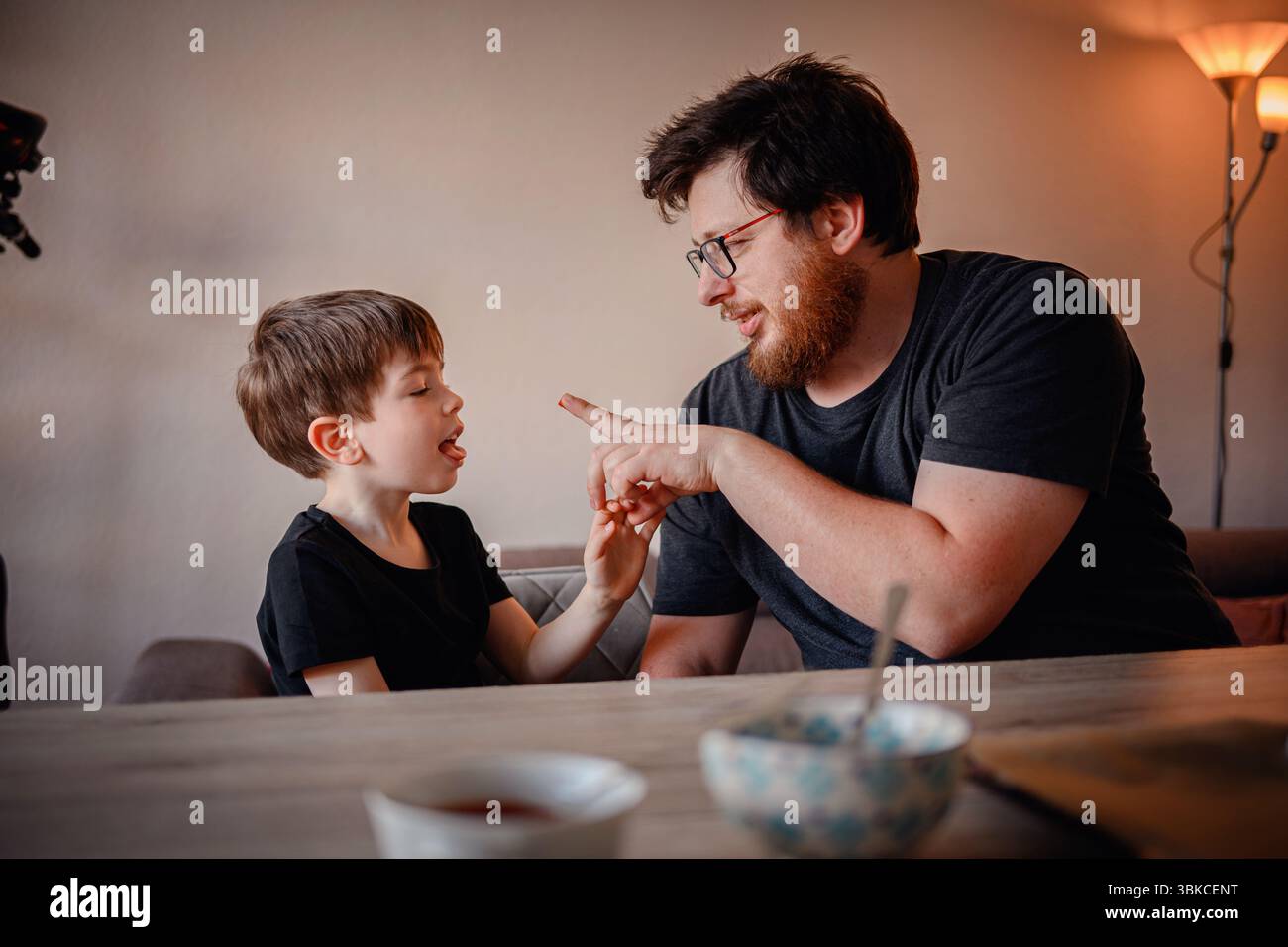 Smiling father gently touches his son's nose as the boy sticks out his ...