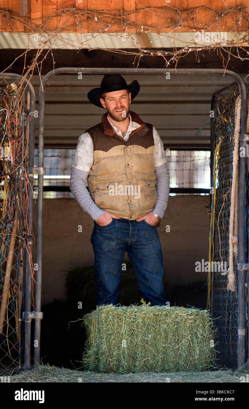 A male ranch hand, wearing western attire and a cowboy hat, takes a ...