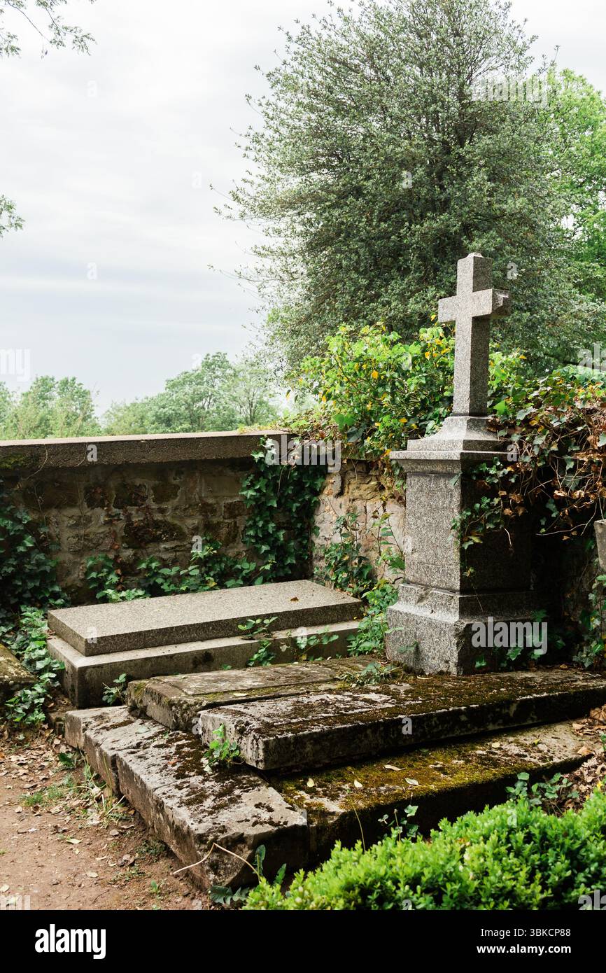 Moss-covered stone graves and cross in a walled cemetery garden Stock ...