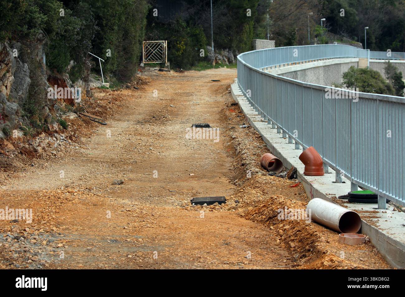 Unfinished gravel path curves alongside a tall metal railing, with ...