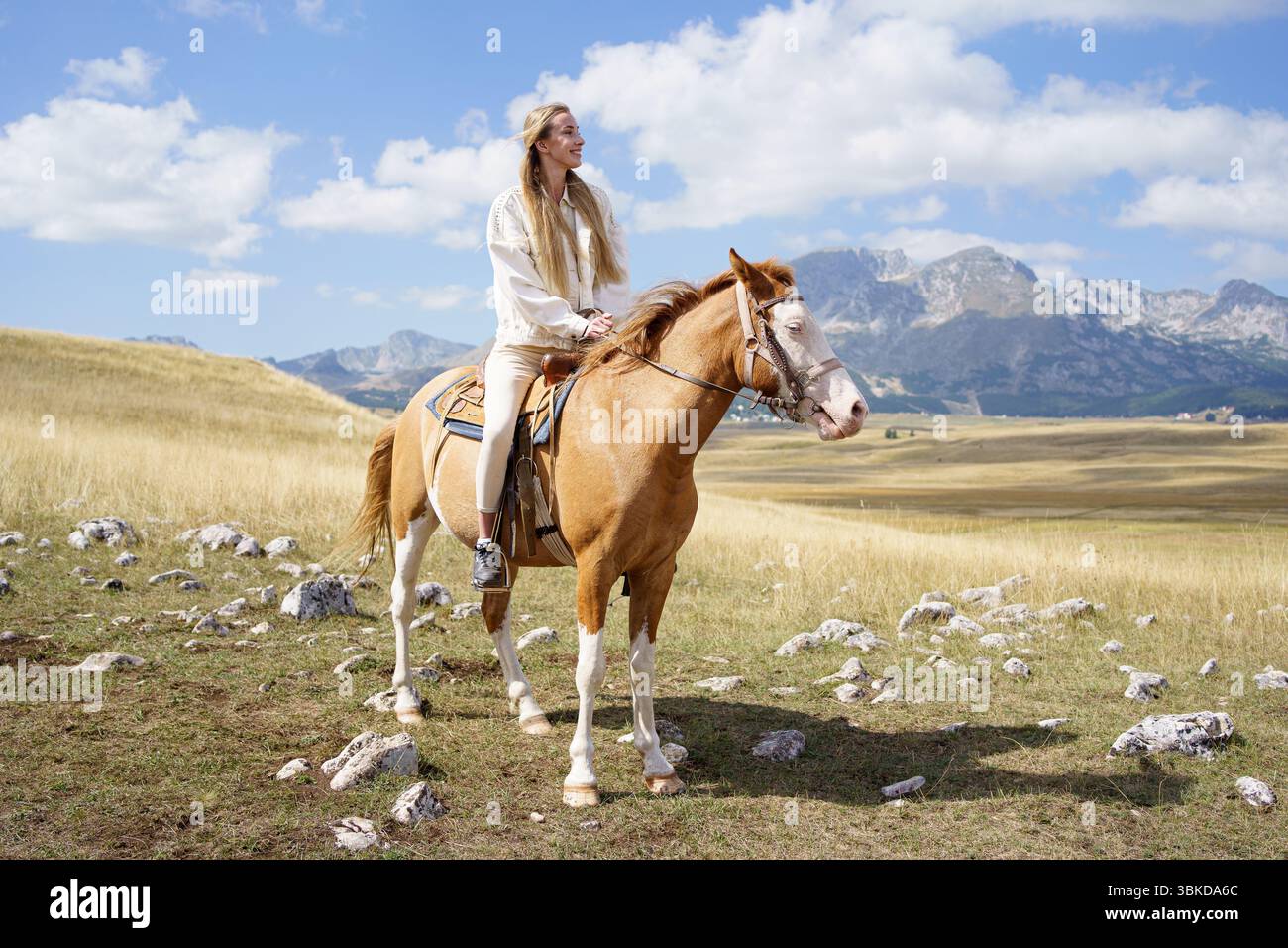 Happy Woman riding horse in open field with mountains in background on ...