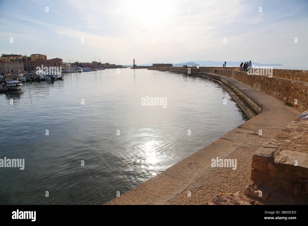 Visitors walk along the stone pier at Chania Harbor, Crete, heading ...
