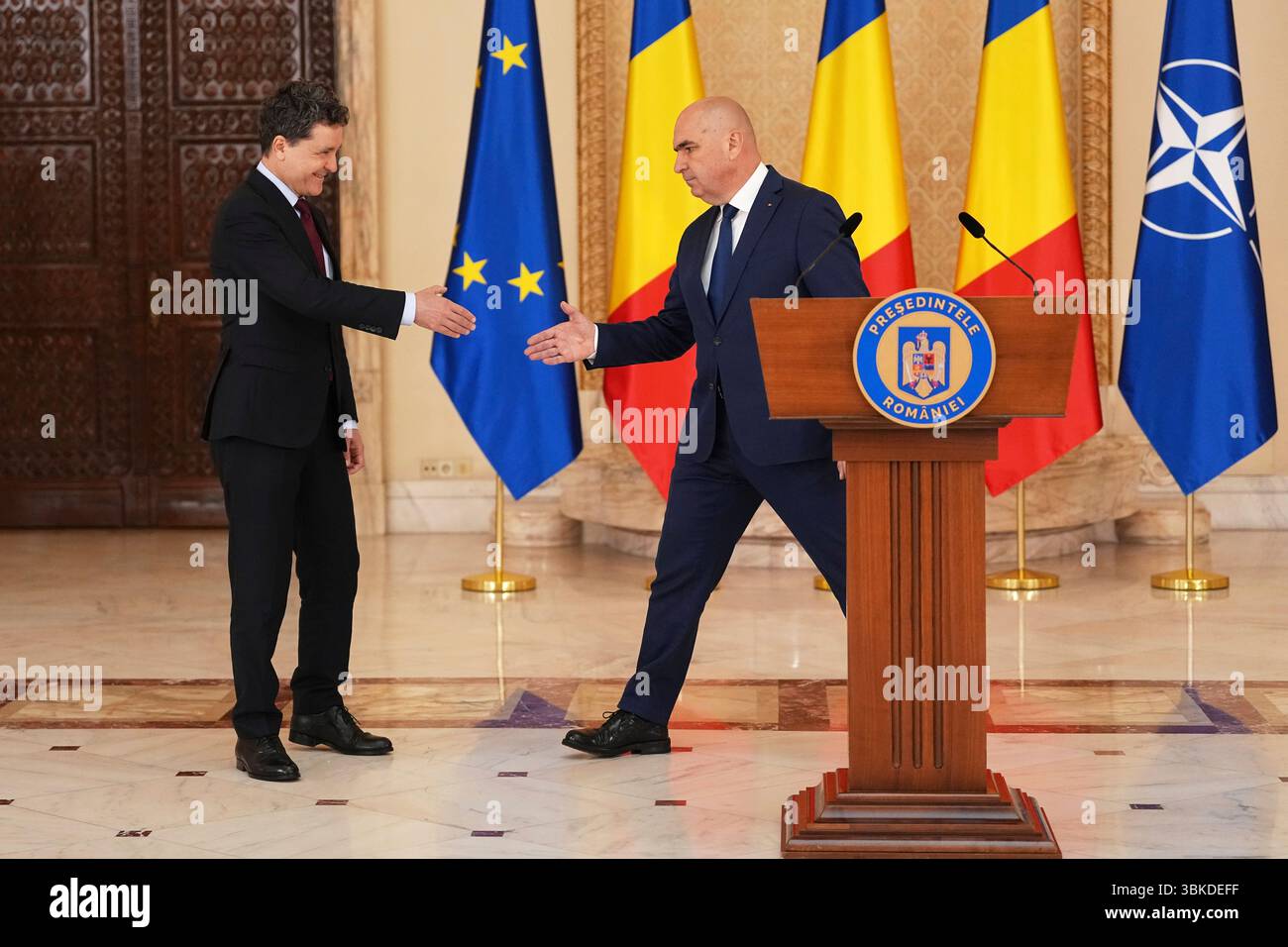 Romanian President Nicusor Dan, left, shakes hands with Ilie Bolojan ...