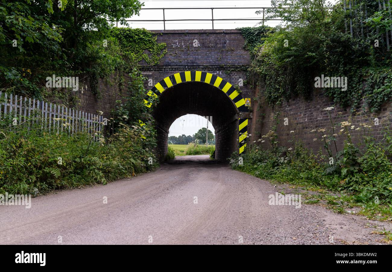 Gravel road passing under a low bridge with black and yellow hazard ...