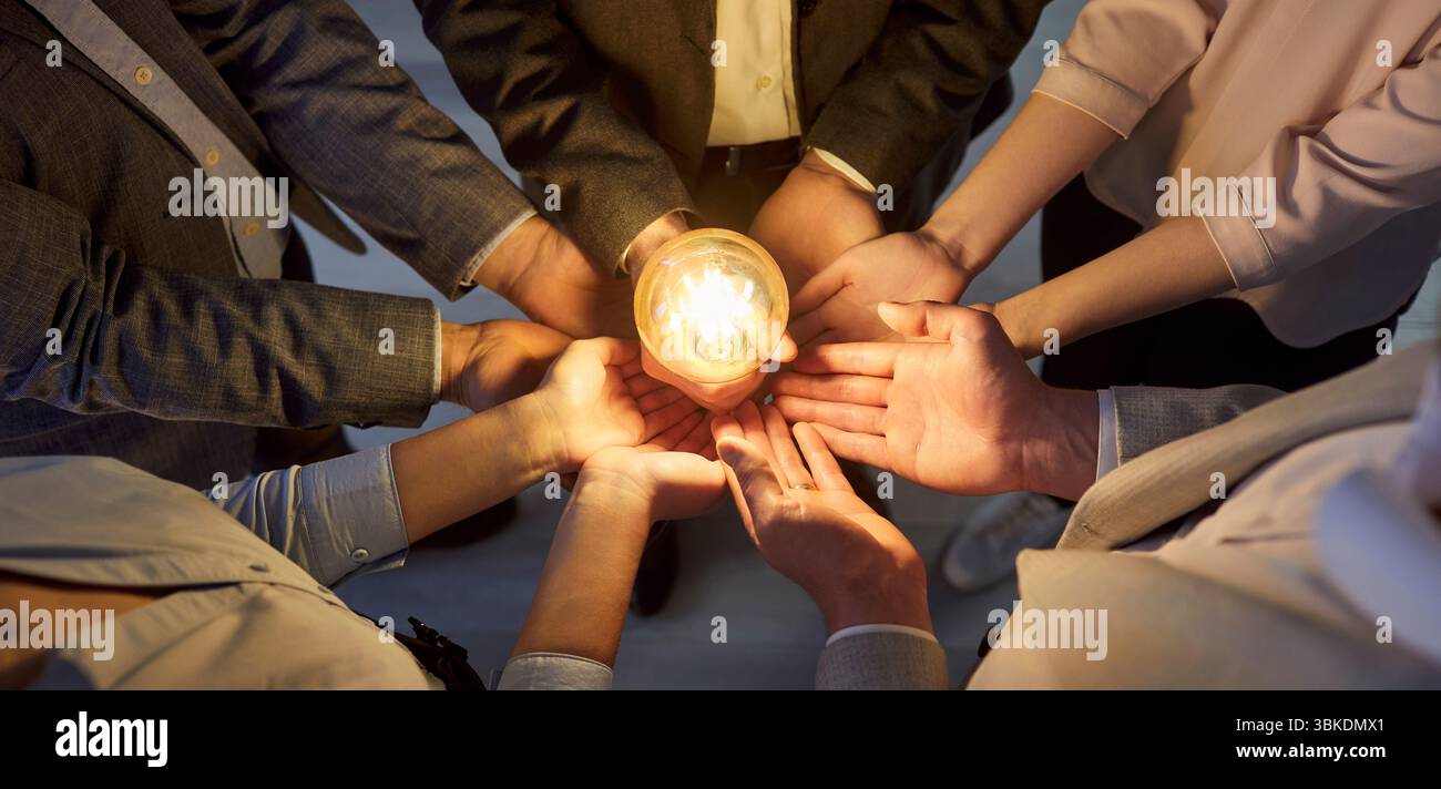 Business team joining hands, holding glowing light bulb, showing ...