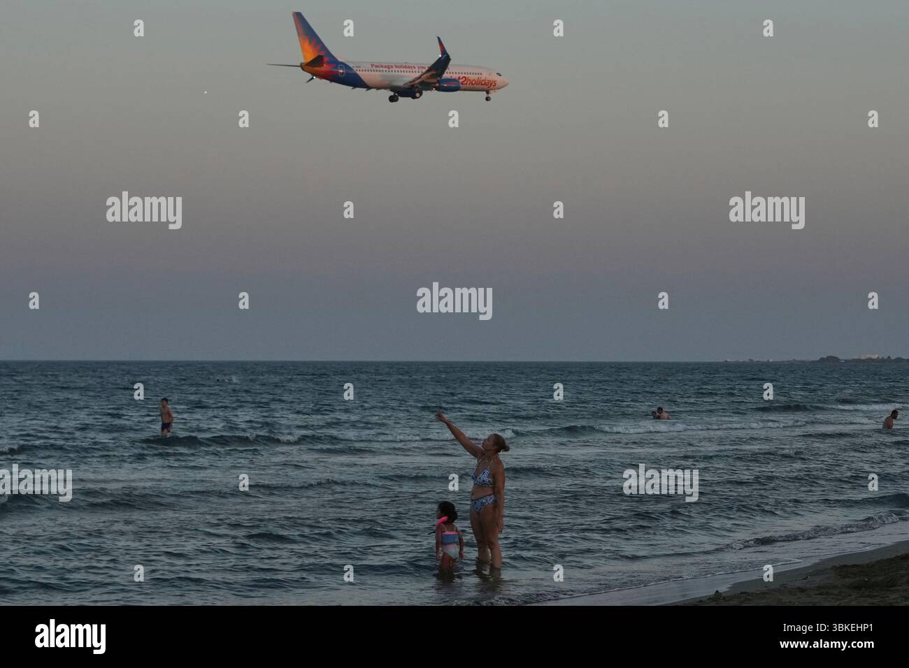 A woman and a child stand in the sea in the afternoon, as an aircraft ...