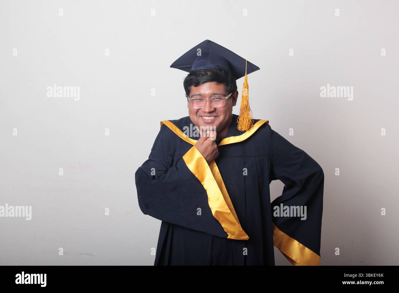 30-year-old dark-skinned Latino man with glasses wears a cap and gown ...