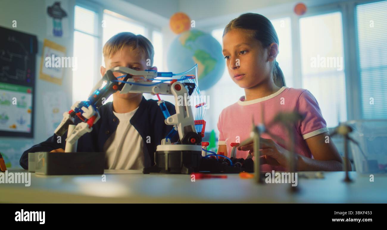 Team of Talented Boy and Girl Sitting at Table, Studying Robotic Arm Model. Primary School ...