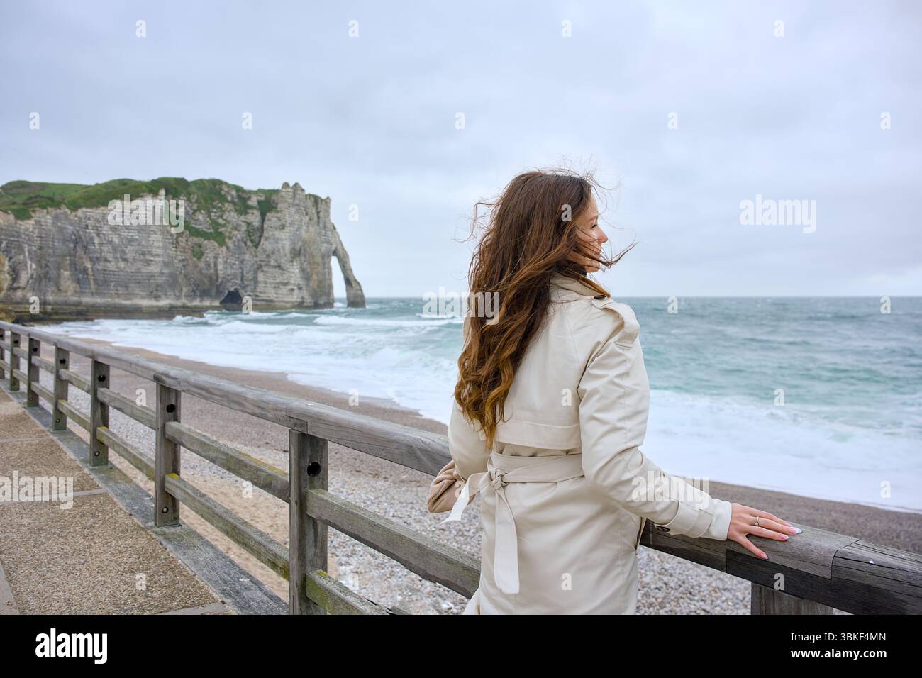 Woman in beige trench looking at Etretat cliff in Normandy Stock Photo ...