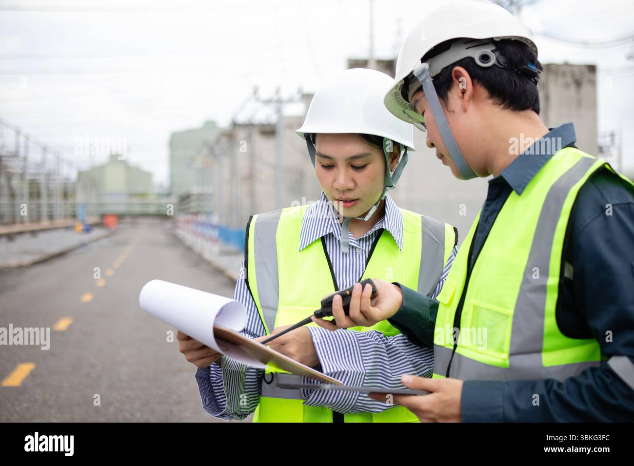 A two engineers work together at power substation with staff wearing ...
