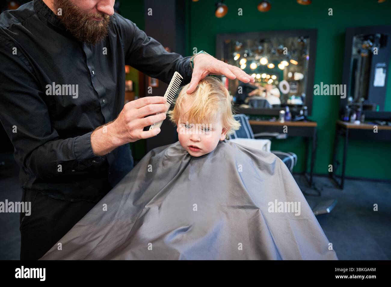 Adorable client ready for new haircut. Professional barber making ...
