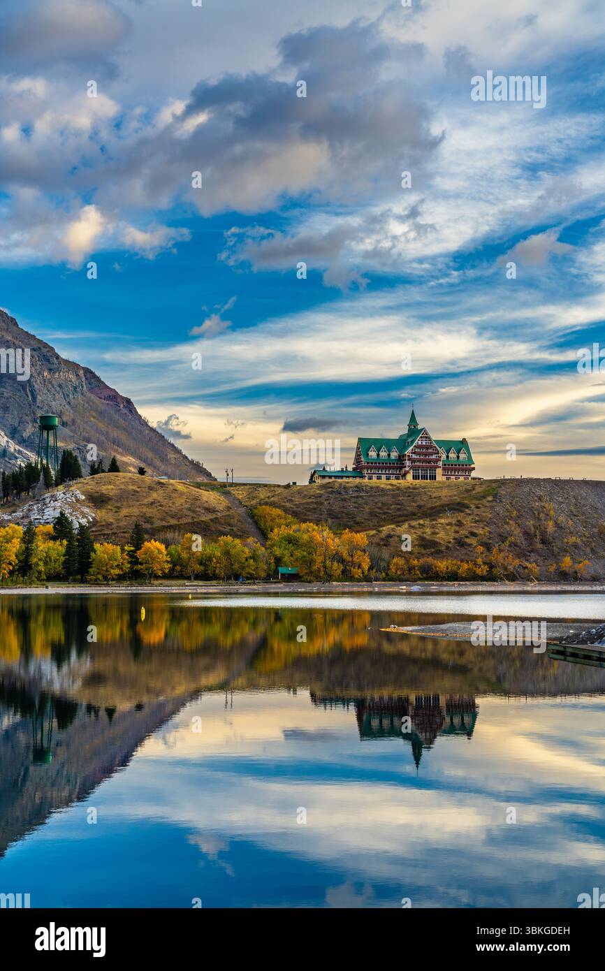 Colorful sunrise clouds reflect on mirror-like Waterton Lake in autumn ...