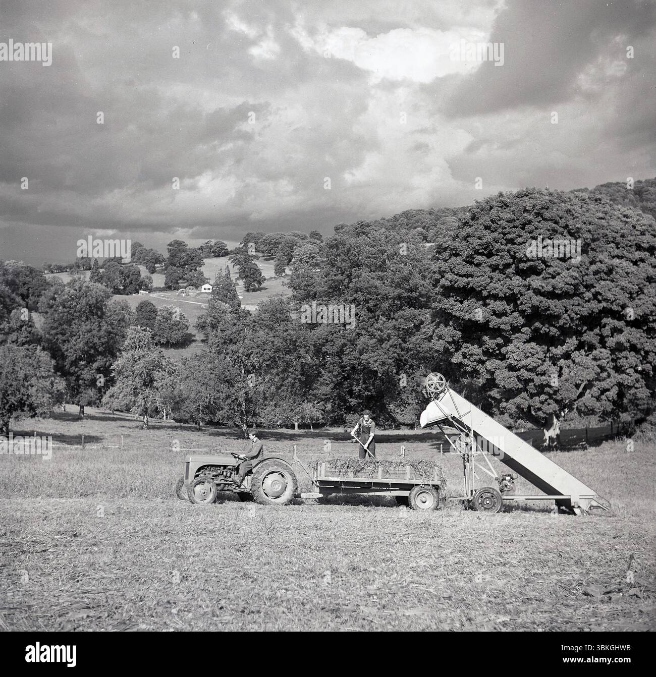 1950s, historical, farmer on tractor, labourer standing on rear trailer ...