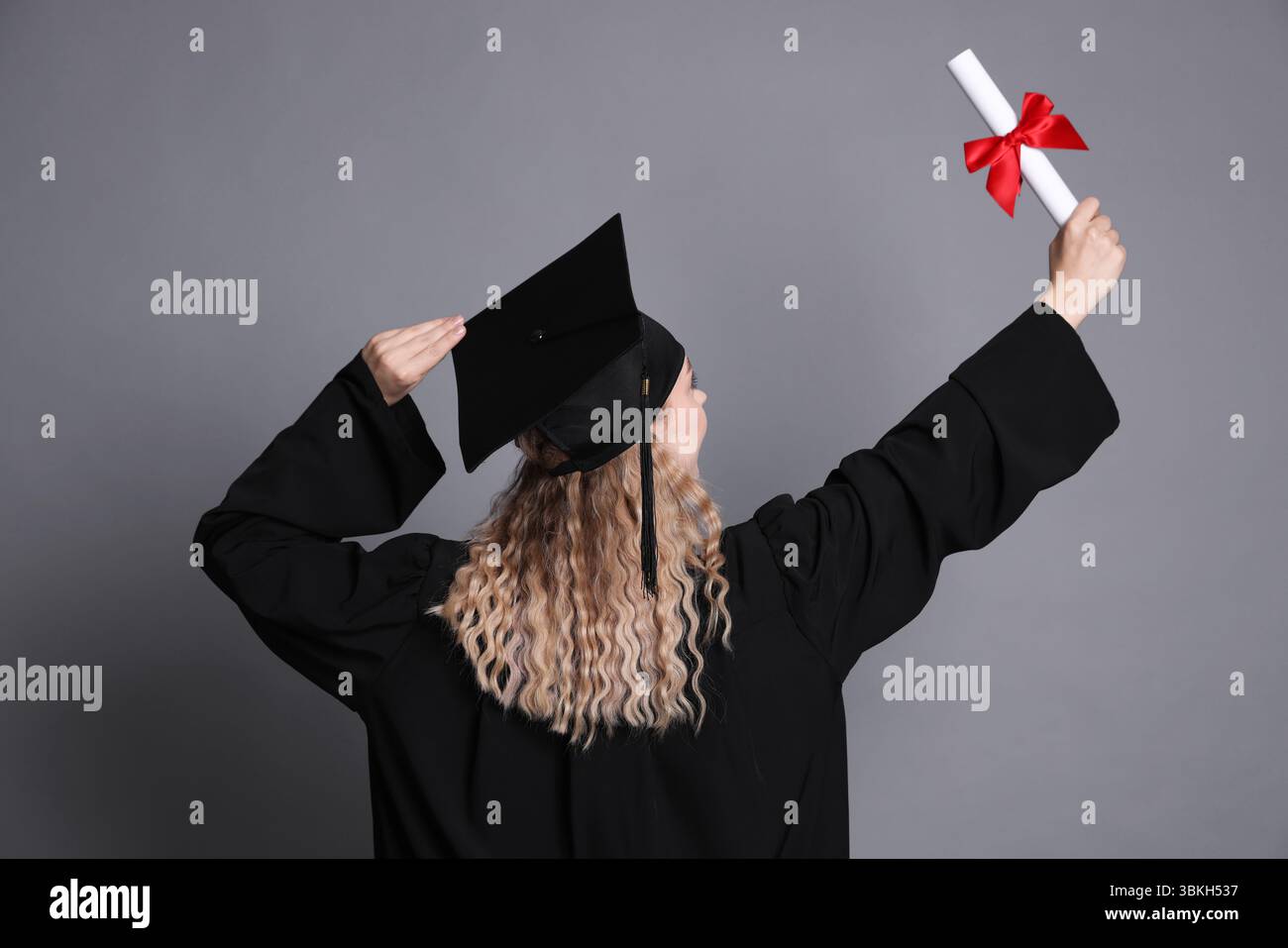 Student in mortarboard with diploma after graduation on grey background ...