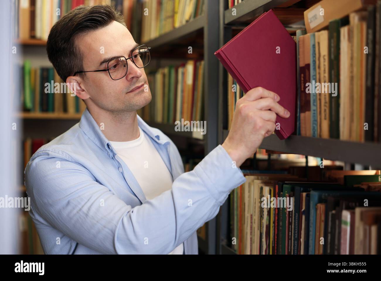 Man taking book from shelf in public library Stock Photo - Alamy