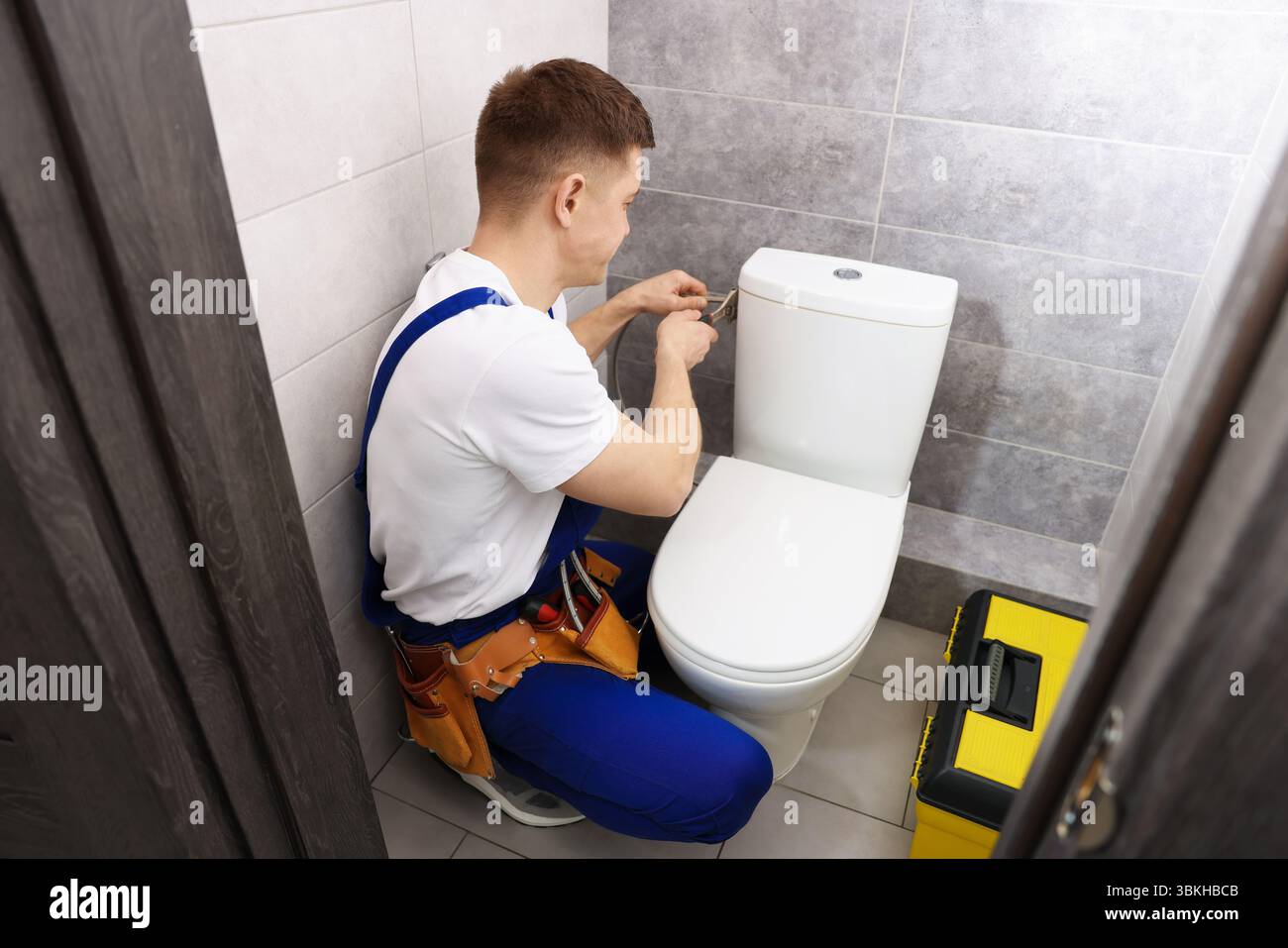 Professional plumber fixing toilet bowl in restroom Stock Photo - Alamy