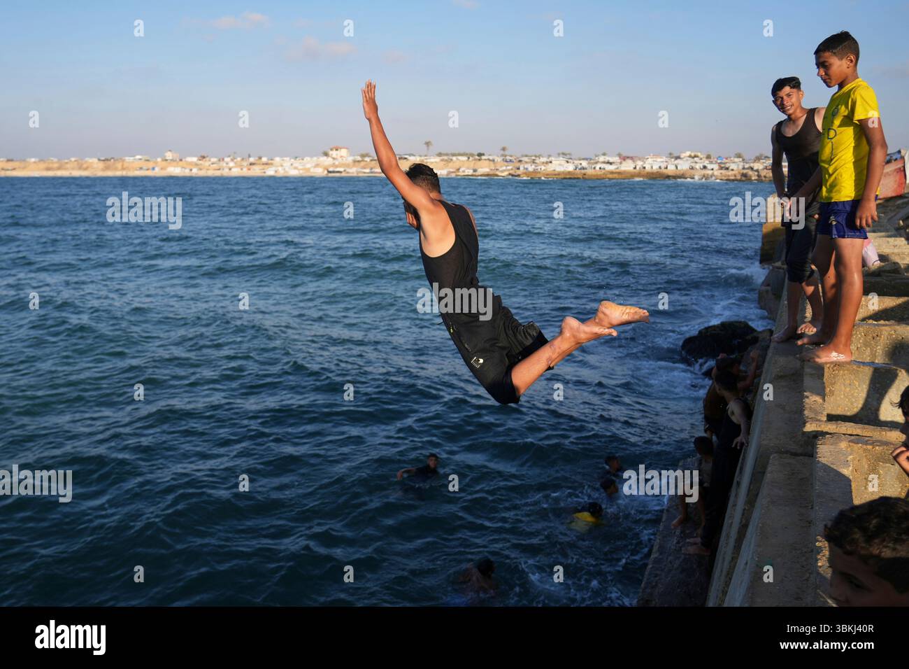 A boy jumps to the Mediterranean Sea next to a makeshift tent camp for ...