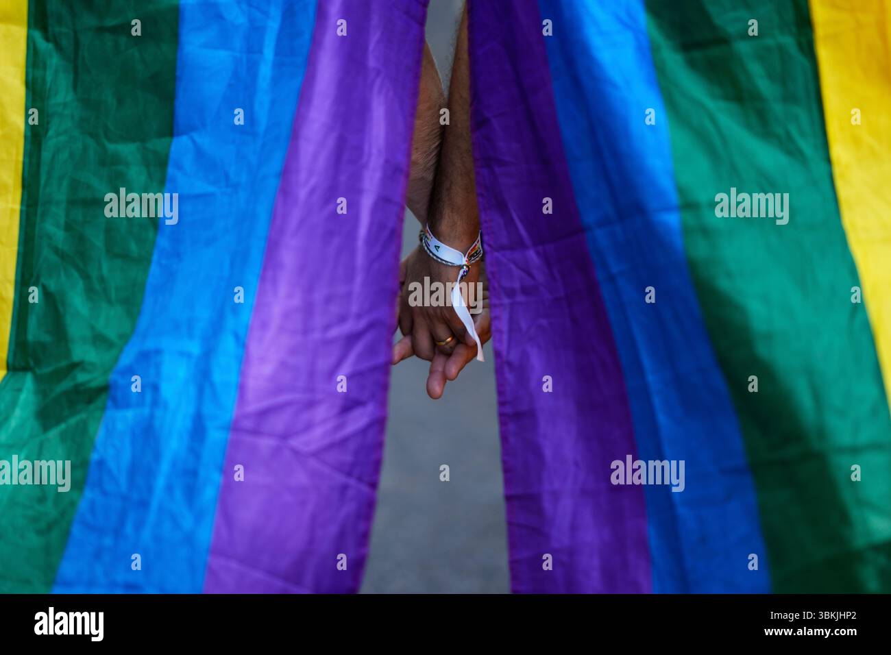 Two men wearing rainbow flags over their shoulders, walk hand-in-hand ...