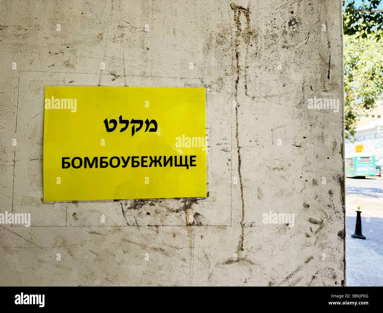A yellow sign with text in Hebrew and Russian indicating a bomb shelter ...