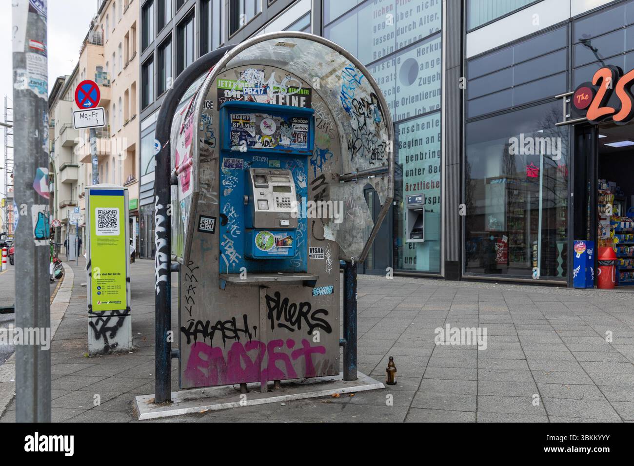 Graffiti-covered public phone booth on a city sidewalk next to a modern ...