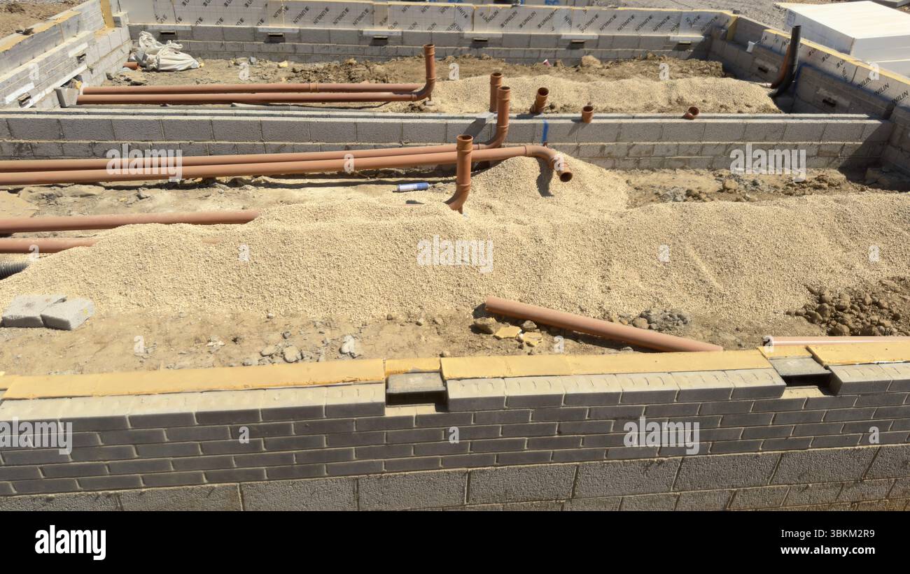 A construction site view of a foundation with pipes and gravel. The ...
