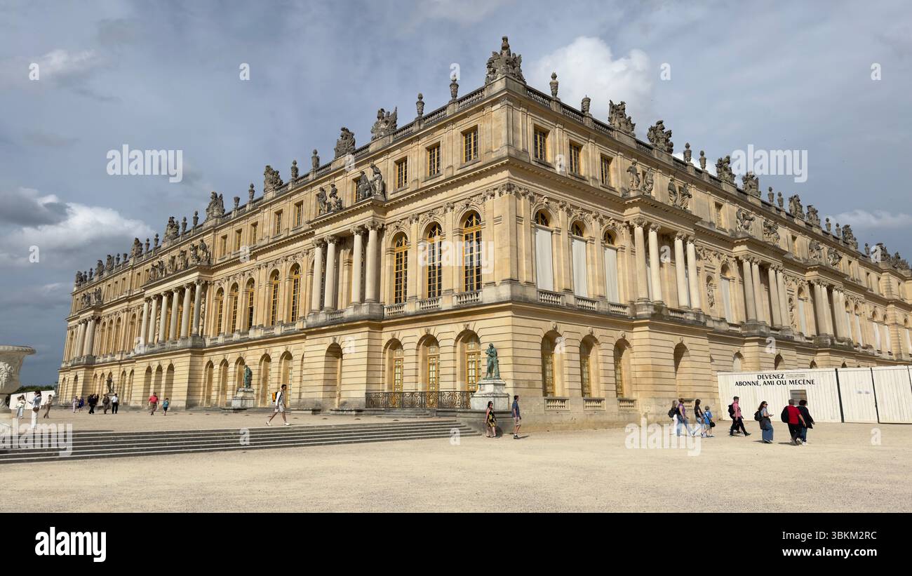 Versailles Palace exterior view with people, stairs, and a cloudy sky ...