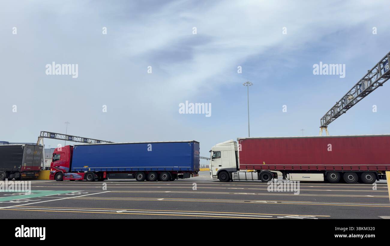 Several semi-trailer trucks parked in a row under a cloudy sky, with ...