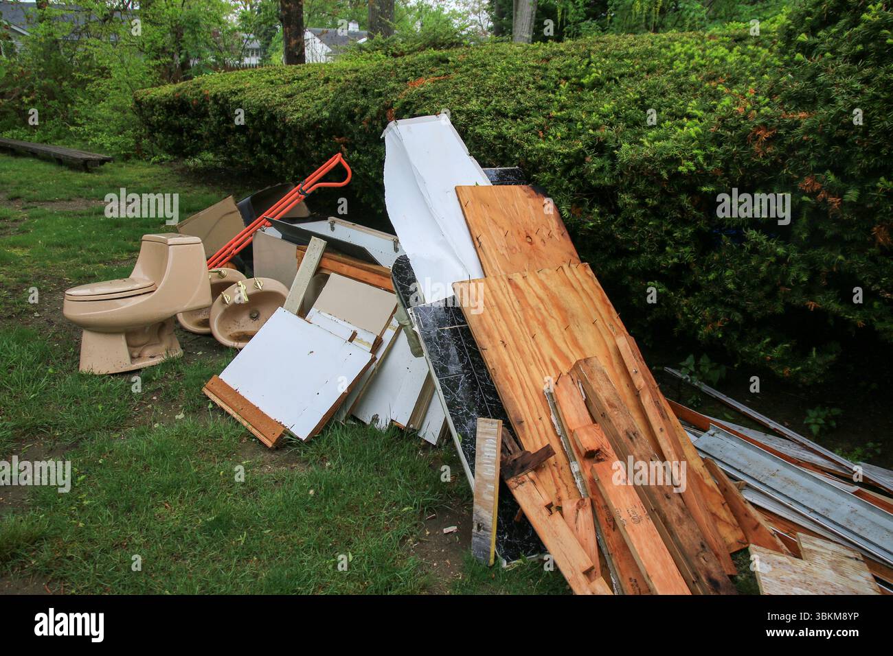 Discarded materials, including a toilet, pile up in a lush green outdoor space Stock Photo - Alamy