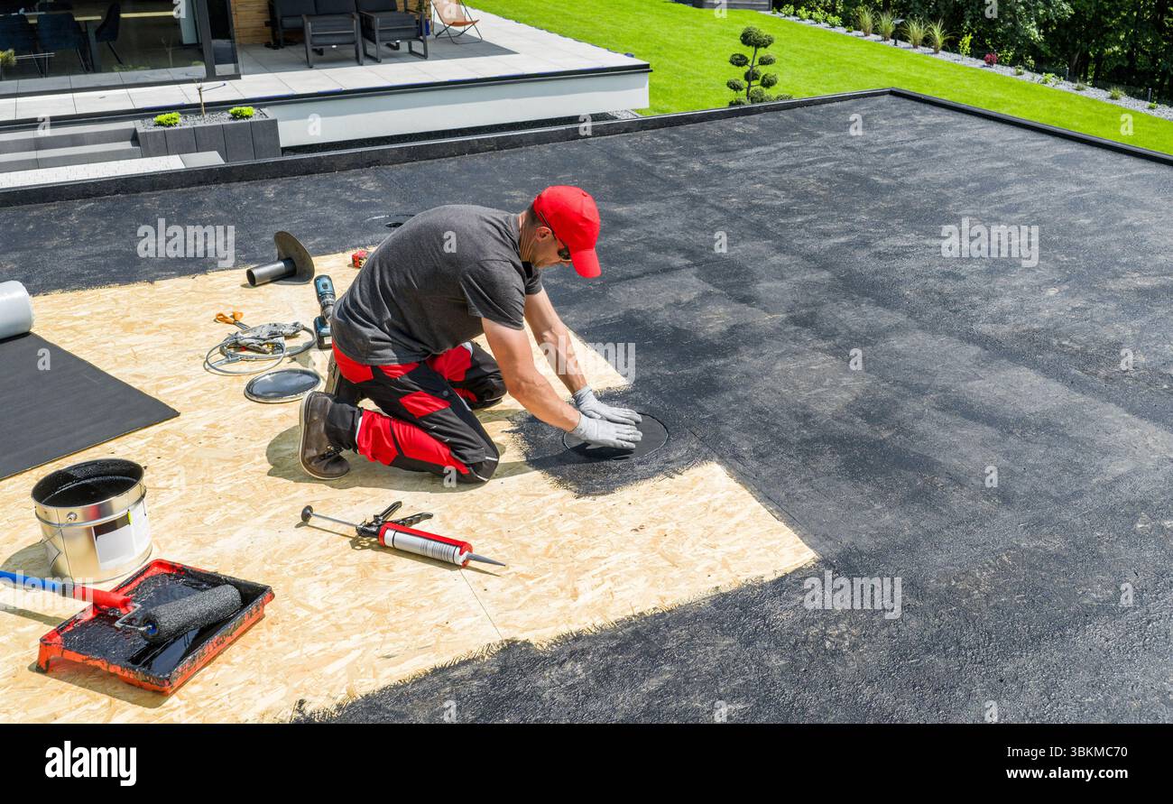 A roofer is working diligently to install a waterproof membrane on a ...