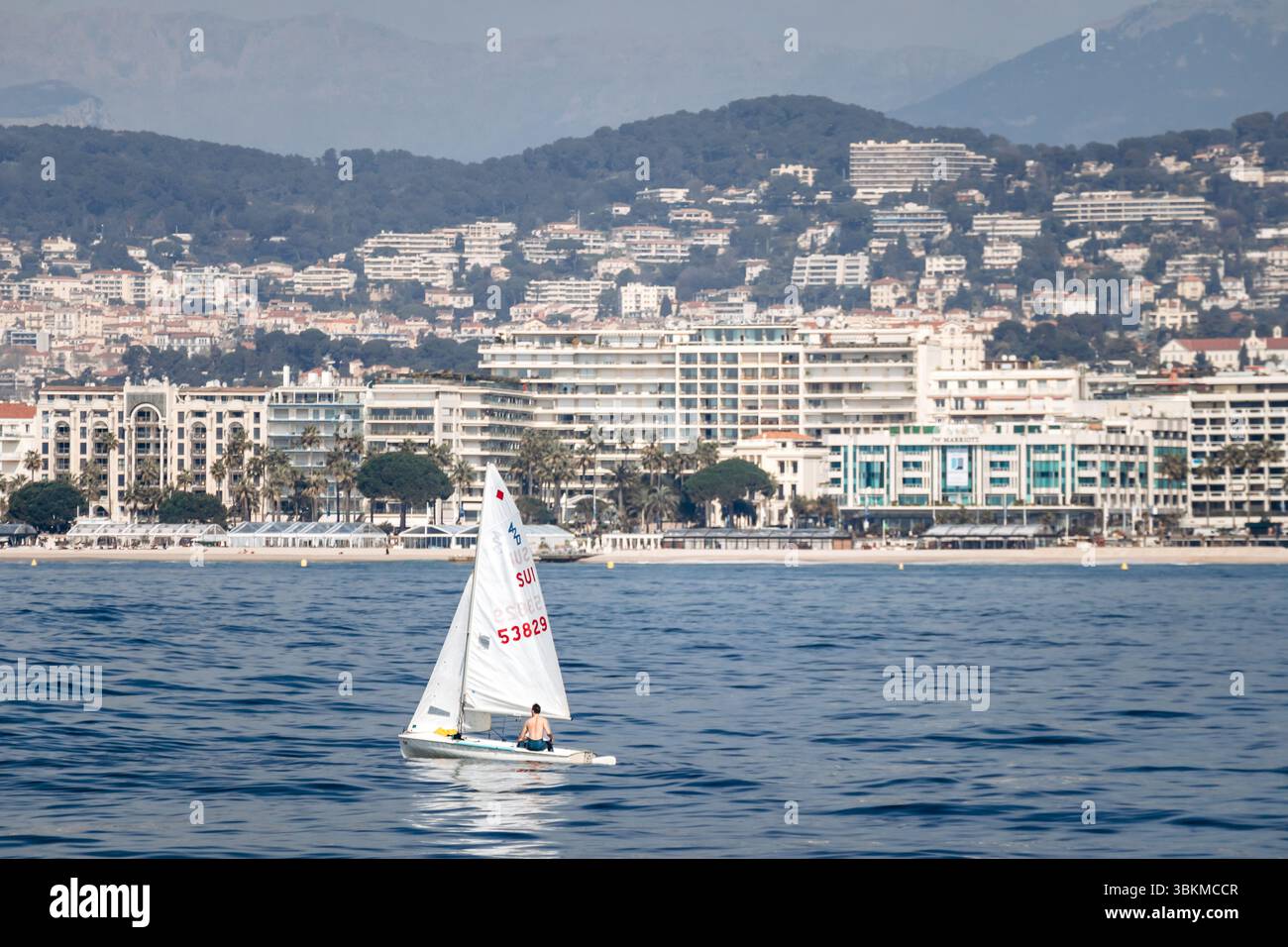 Cannes, France - March 8, 2025: Sailboat on the calm sea with cityscape ...