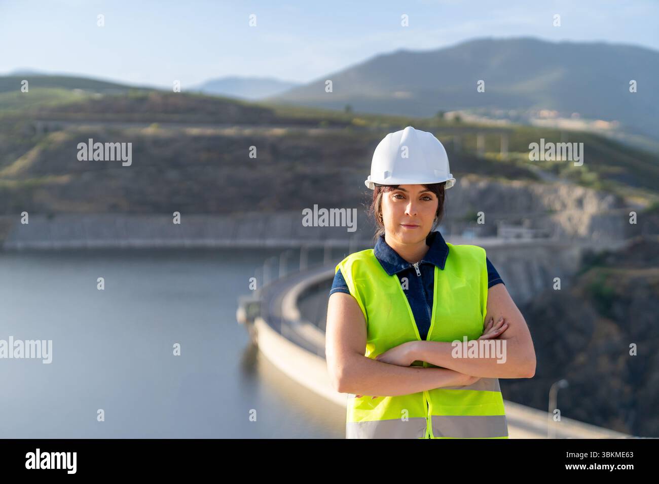 Female engineer overseeing a reservoir dam project with arms crossed ...